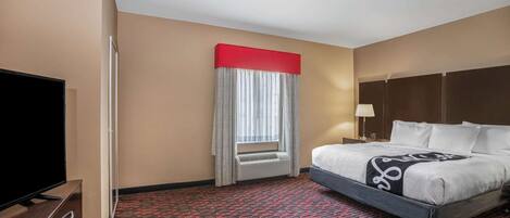 Quarto de hotel com cama, televisão, aquecedor e janela com cortinas.