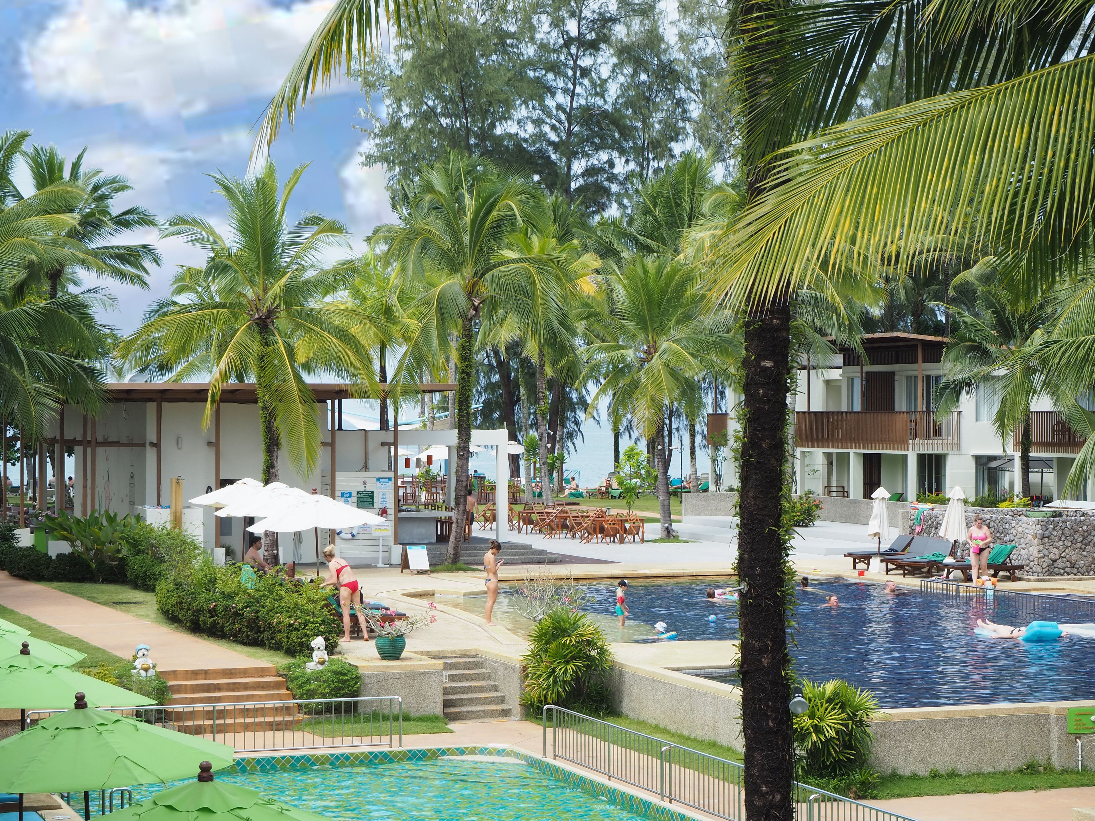 Uma área de piscina em resort com palmeiras, espreguiçadeiras e um edifício com varandas.