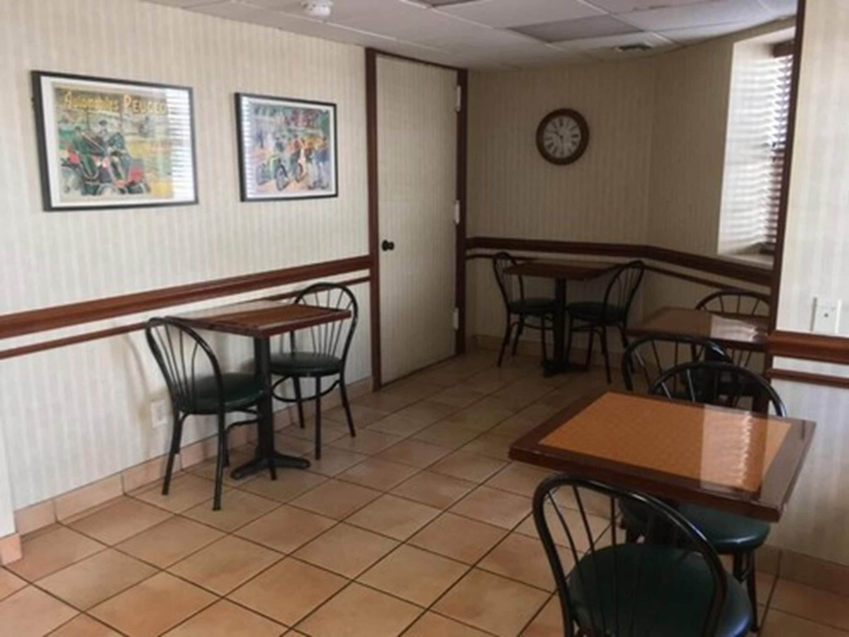 Um restaurante com chão de azulejos, mesas e cadeiras de madeira e duas molduras na parede.