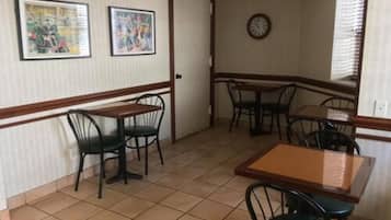 Um restaurante com chão de azulejos, mesas e cadeiras de madeira e duas molduras na parede.