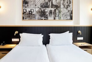 Quarto de hotel com duas camas, cabeceira preta, abajures e uma grande obra de arte abstrata na parede.