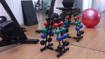 Academia com equipamentos de ginástica, incluindo esteira, aparelhos de musculação e uma bola de exercício vermelha grande.