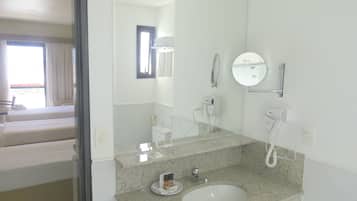 Casa de banho de hotel com bancada de granito, pia, espelho, porta-toalhas e secador de cabelo.