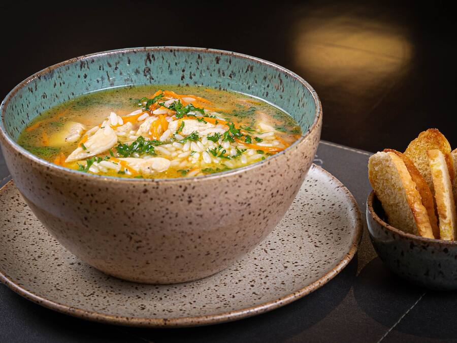 Uma tigela de sopa acompanhada de pão em um prato.