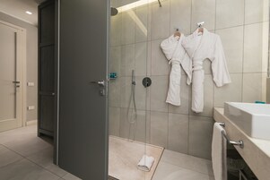 Casa de banho moderna com cabine de duche em vidro, lavatório branco e duas toalhas brancas penduradas em ganchos.