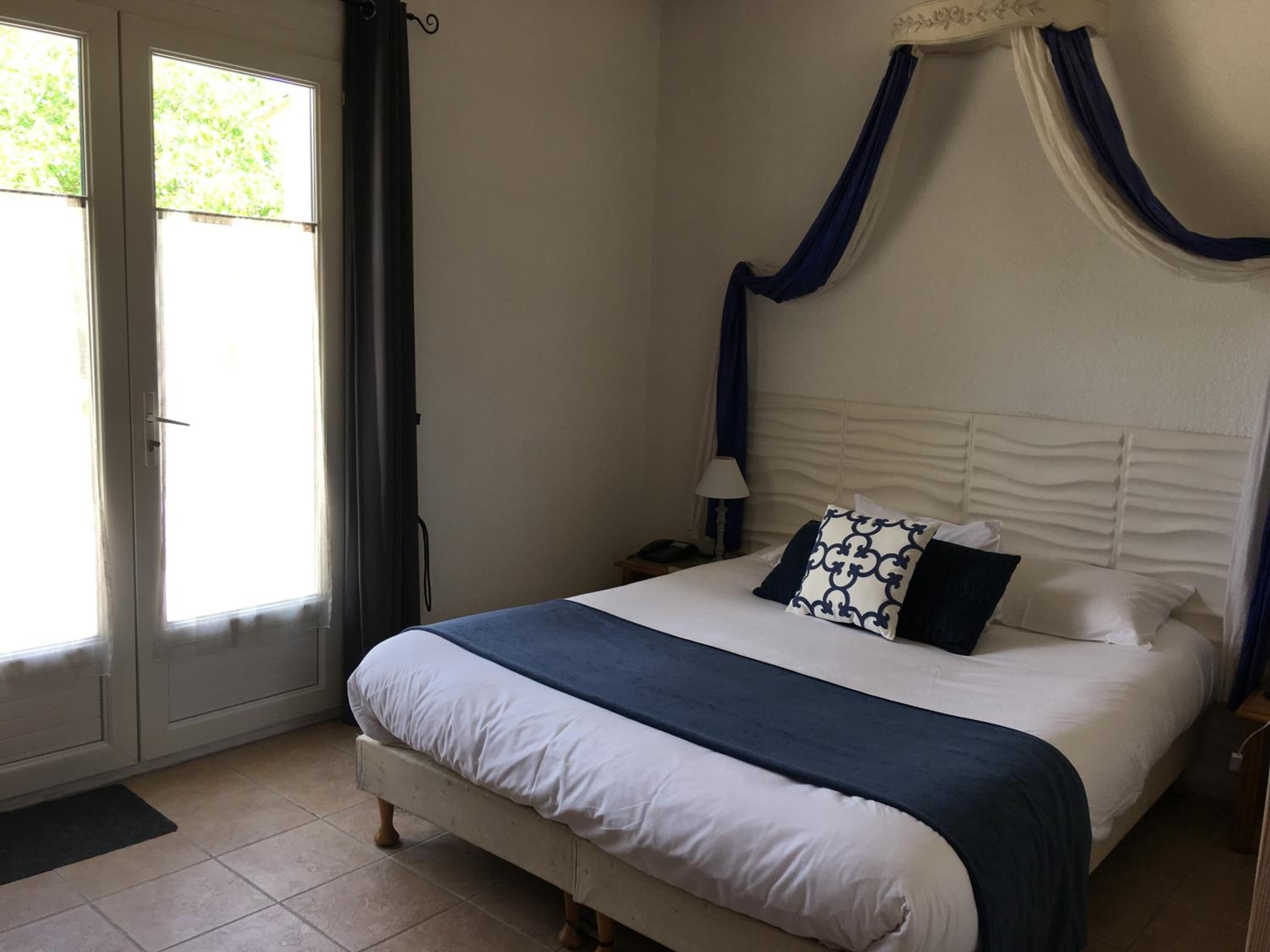 Quarto com cama, mesa de cabeceira, abajur e janela com cortinas.