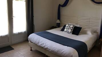 Quarto com cama, mesa de cabeceira, abajur e janela com cortinas.