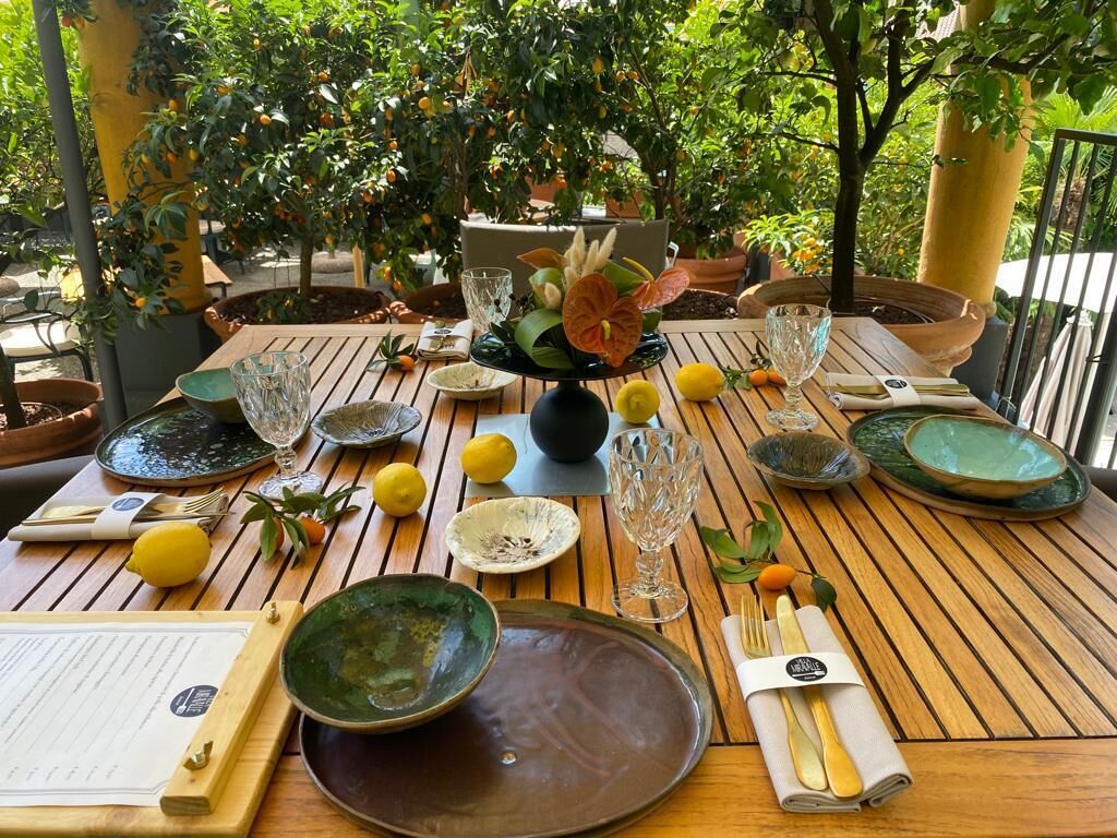 Uma mesa de madeira posta para refeição, com pratos, copos e um centro de mesa.