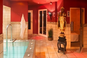 Um quarto de spa com banheira, uma estátua, um porta-toalhas e uma porta de madeira.