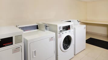 Uma lavanderia com três secadoras industriais e uma máquina de lavar.