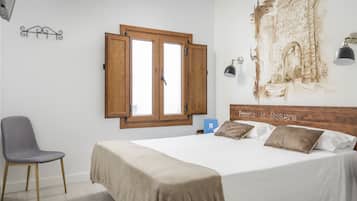 Quarto com cama, poltrona, janela com persianas de madeira e um mural na parede.