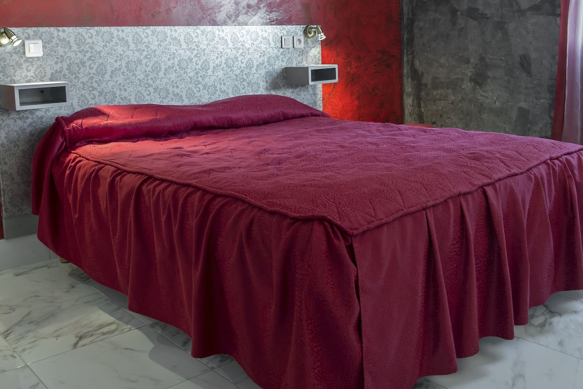 Quarto moderno com cama, piso de mármore e parede decorada em vermelho.