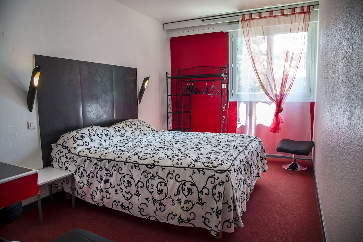 Um quarto com cama, escrivaninha, cadeira, guarda-roupa e janela com cortina.