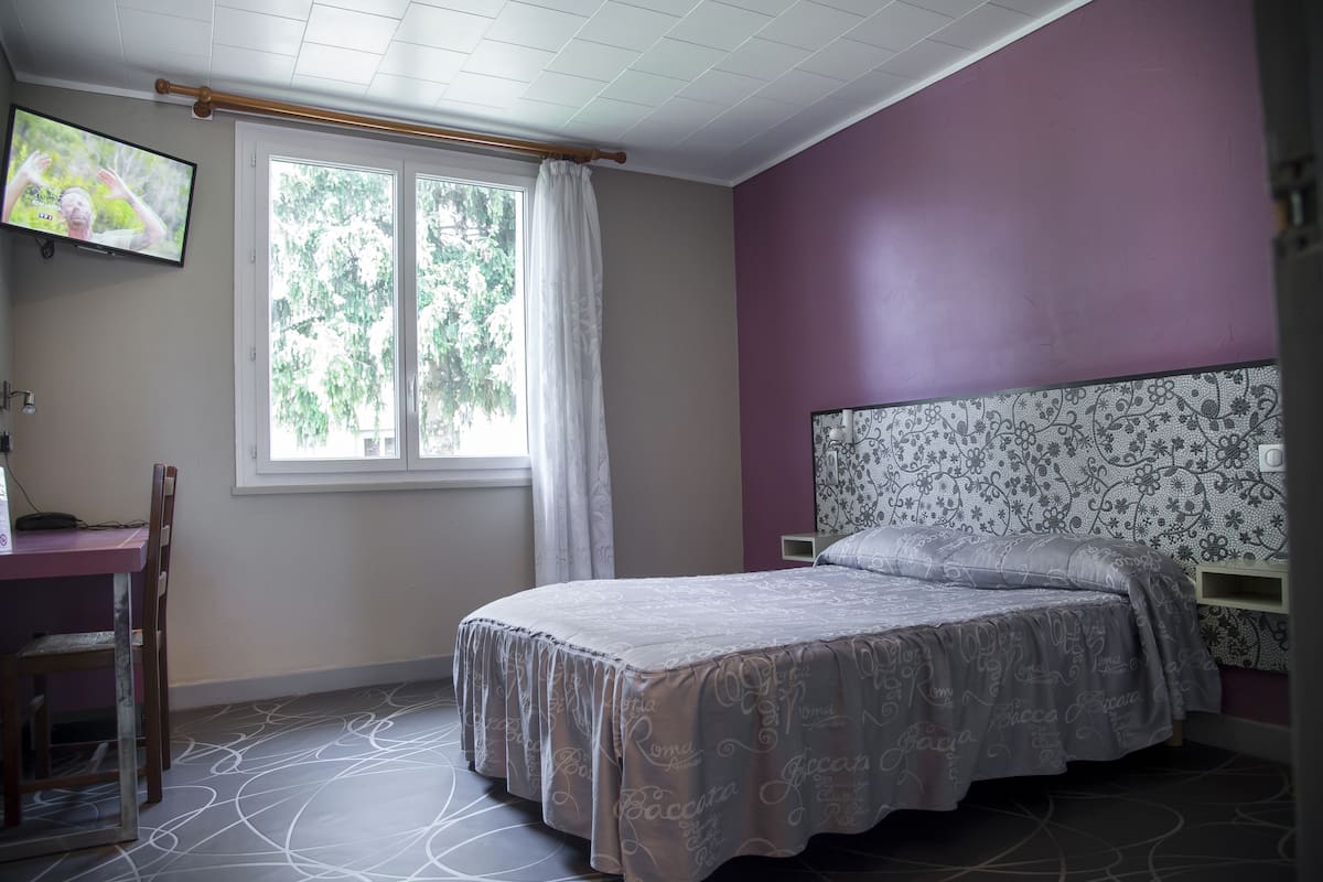 Quarto com cama, escrivaninha e televisão.