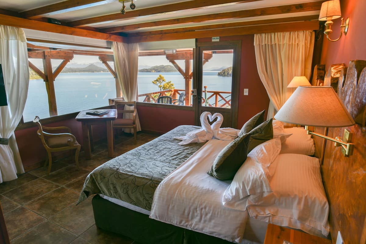 Quarto com cama, escrivaninha e vista para um lago.