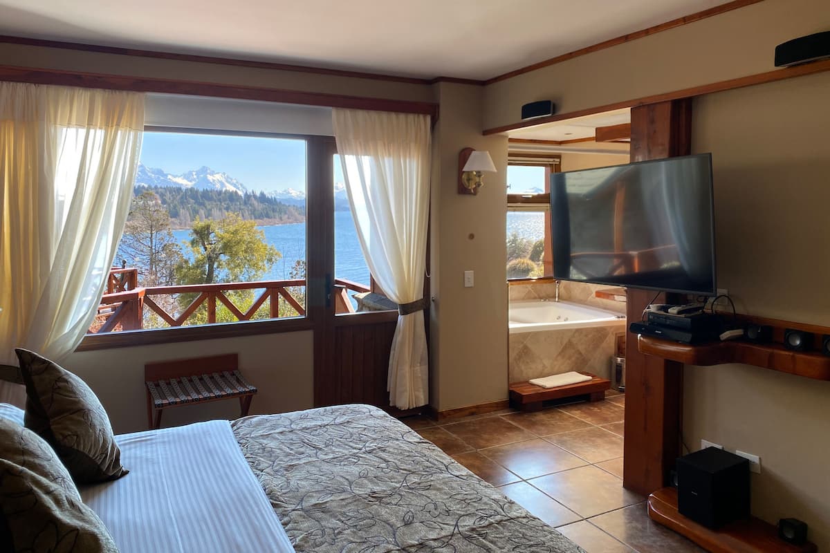 Quarto com uma janela grande, cama, televisão, banheiro e um deck de madeira.