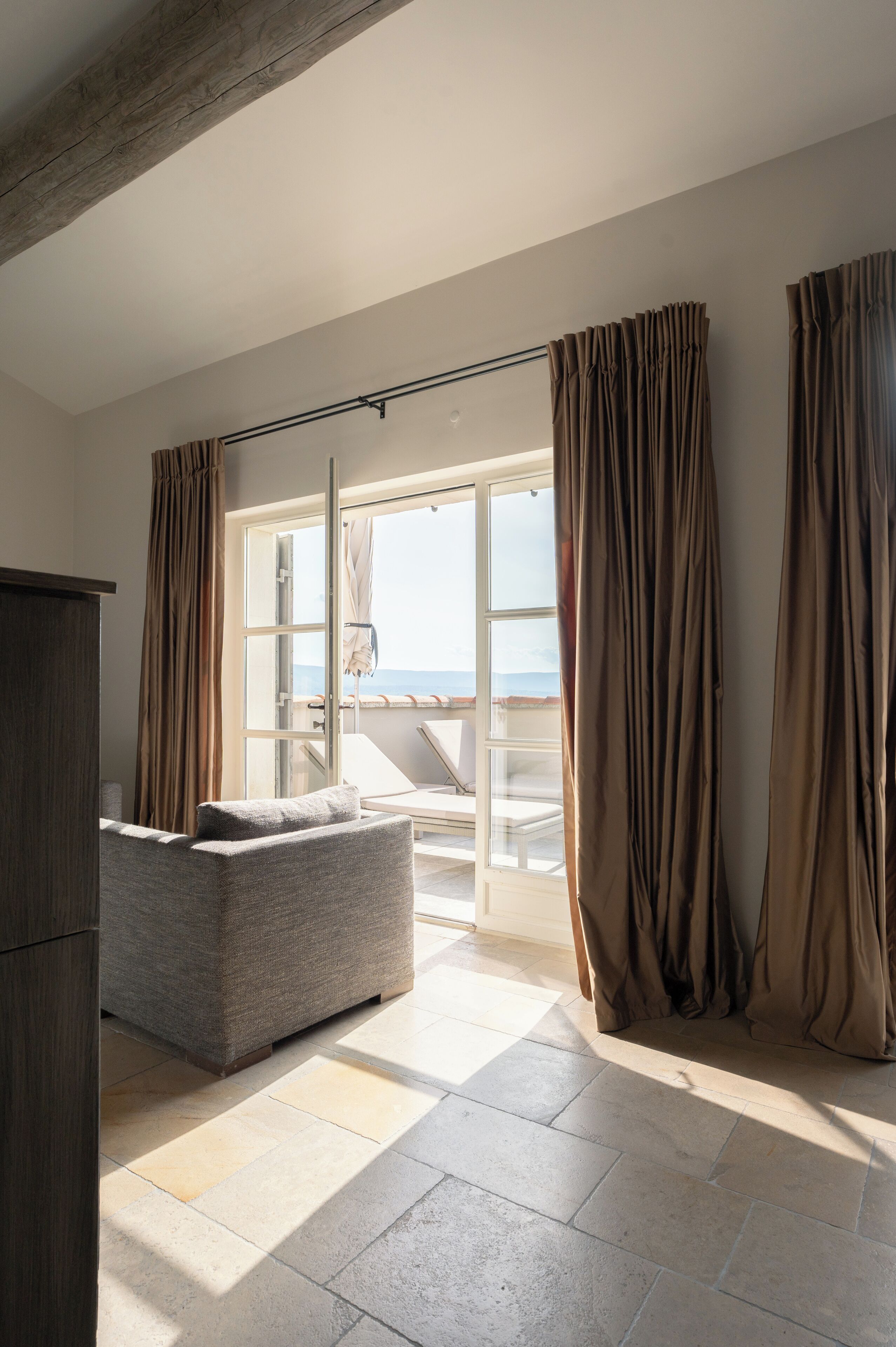 Um quarto espaçoso com uma grande porta de vidro deslizante que dá para uma varanda com vista para o mar. Há um sofá e um armário de madeira no quarto.