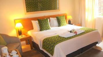 Quarto de hotel com uma cama, duas mesas de cabeceira com luminárias, uma cadeira e uma mesinha com uma bandeja de objetos.
