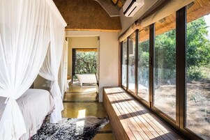 Quarto com cama de dossel, vista para uma floresta e uma janela grande.