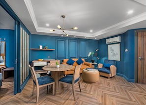 Uma sala de estar moderna com piso de madeira em padrão herringbone, uma mesa redonda de madeira e cadeiras estofadas em azul.