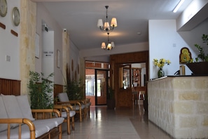 Uma área de recepção com balcão, cadeiras, um candelabro e uma parede com relógio e sinalização.