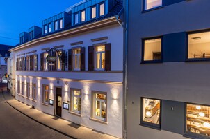 Um edifício de dois andares com janelas iluminadas e um restaurante visível no andar térreo.