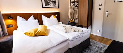 Quarto de hotel com cama bem arrumada, mesa de cabeceira com abajur, cabideiro e quadro na parede.