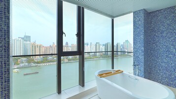 Um banheiro moderno com uma banheira grande, vista para o horizonte urbano e um rio com barcos.
