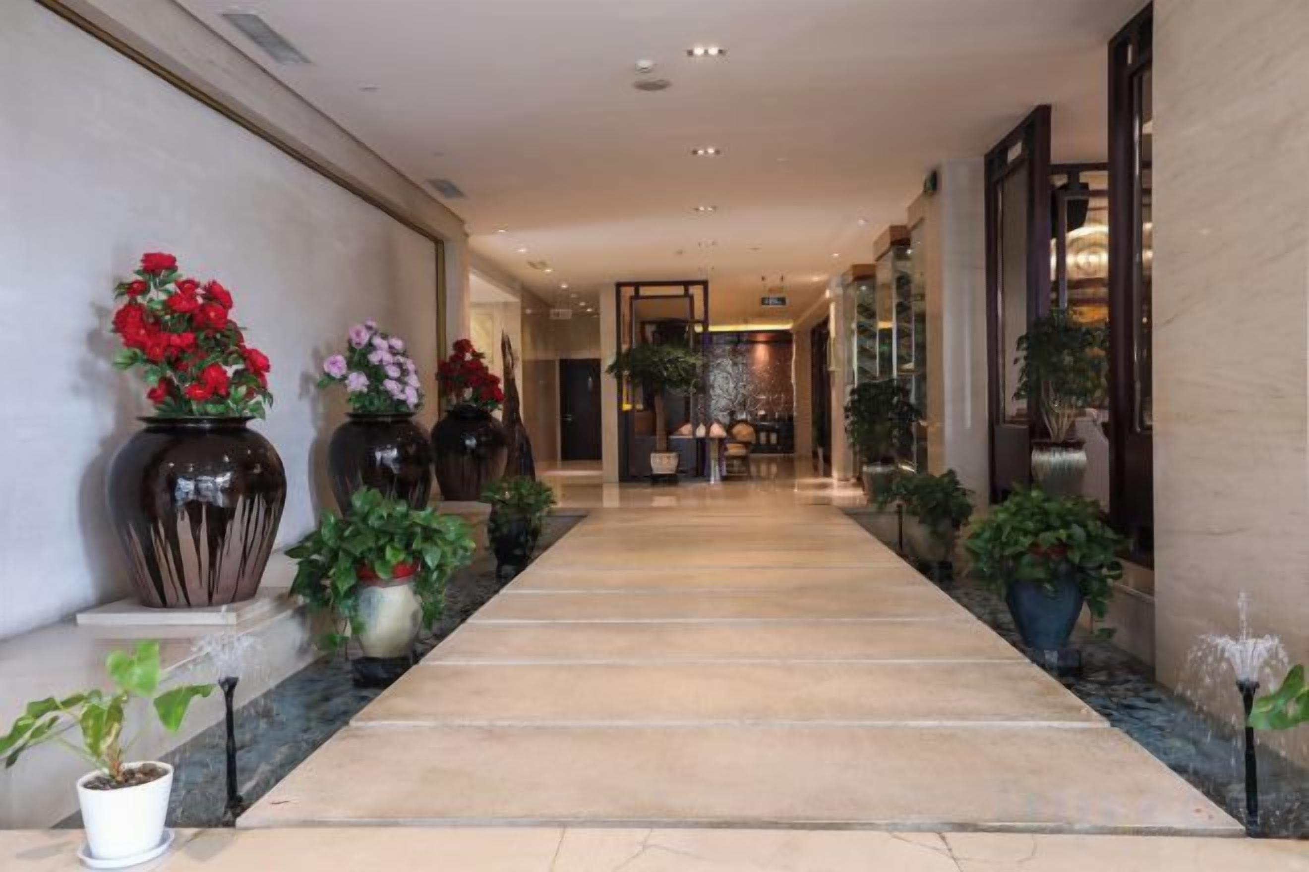 Corredor de hotel com plantas em vasos e piso de mármore.