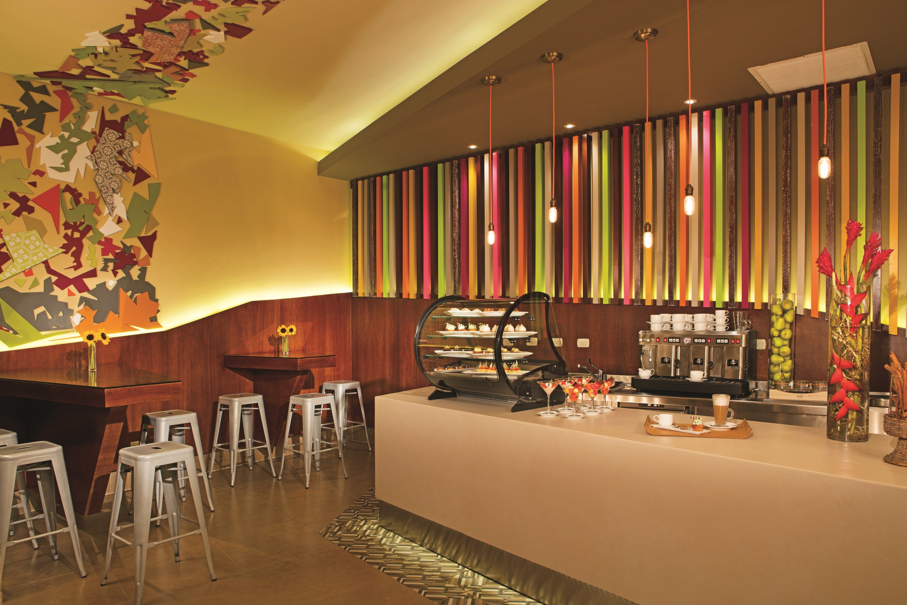 Uma área de bar moderna com uma parede colorida listrada, um balcão de sobremesas e uma máquina de café.
