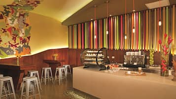 Uma área de bar moderna com uma parede colorida listrada, um balcão de sobremesas e uma máquina de café.
