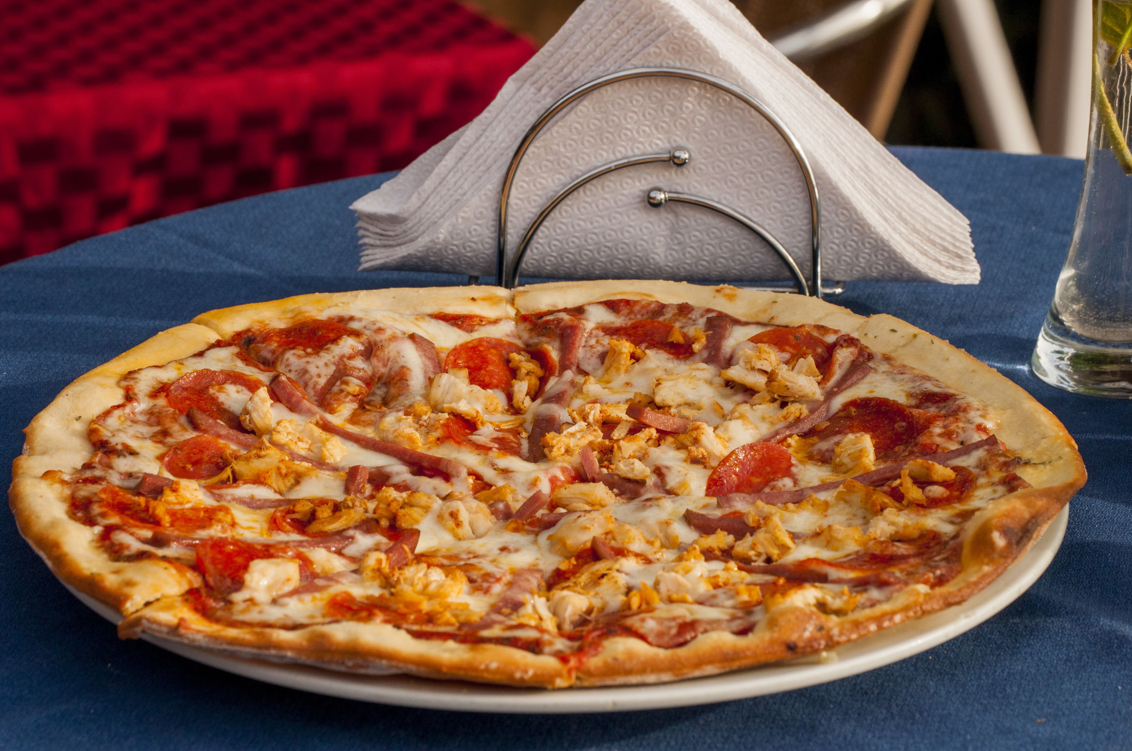 Pizza com diversos ingredientes numa placa branca, colocada sobre uma toalha de mesa azul.
