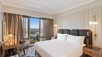 Quarto de hotel com uma cama grande, uma escrivaninha com abajur, telefone e vista para a cidade.