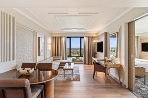 Quarto de hotel com sofá, mesa de jantar, televisão e vista da cidade.