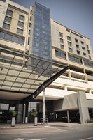 Um hotel de vários andares com fachada de vidro moderna, entrada coberta e área de estacionamento.