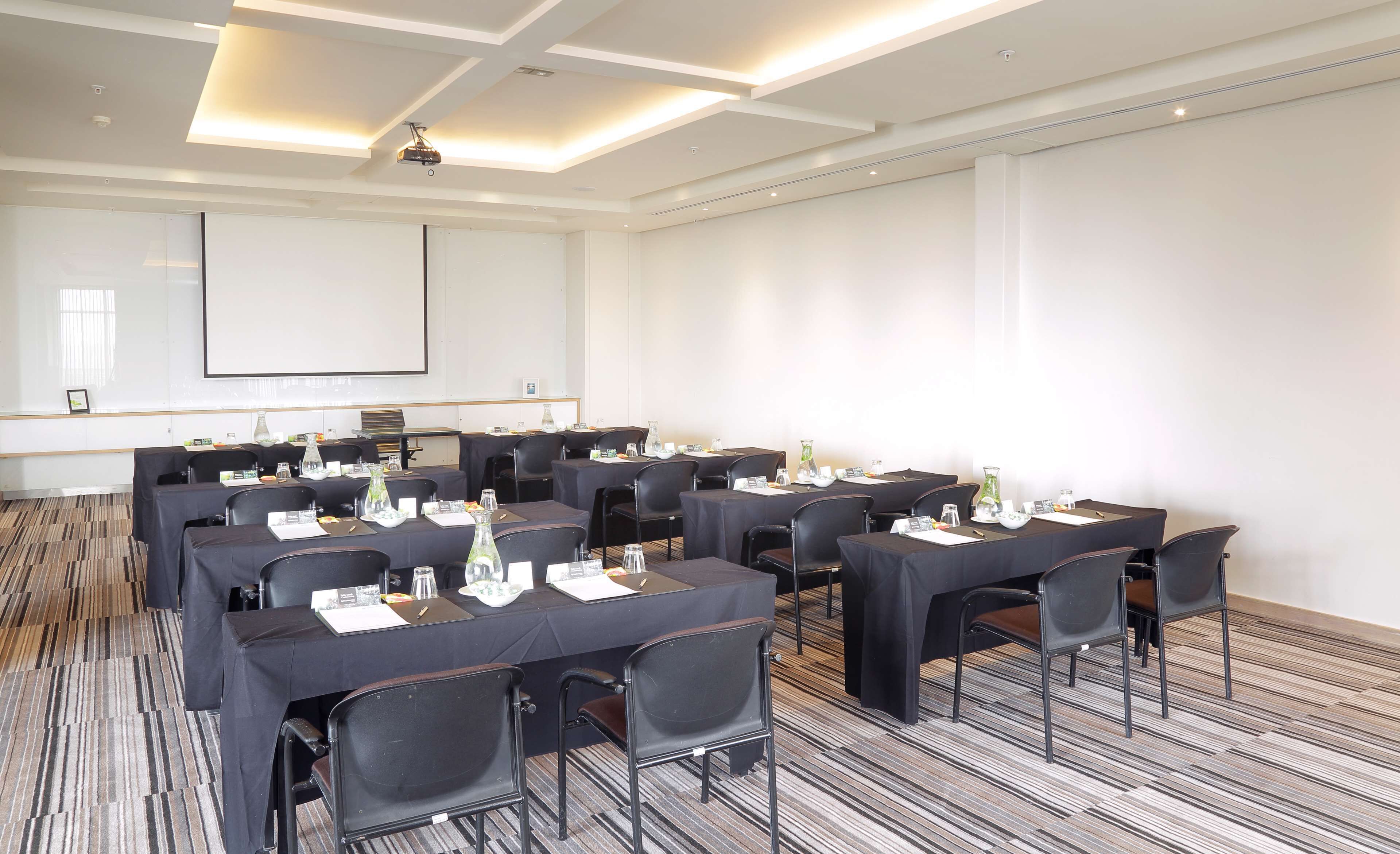 Uma sala de conferências com várias mesas e cadeiras, equipada com porta-nomes, garrafas de água e uma tela de projetor.