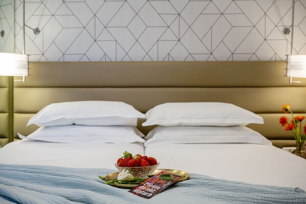 Cama bem arrumada com lençóis brancos, uma tigela de morangos, um tabuleiro com uma revista e um vaso com flores.