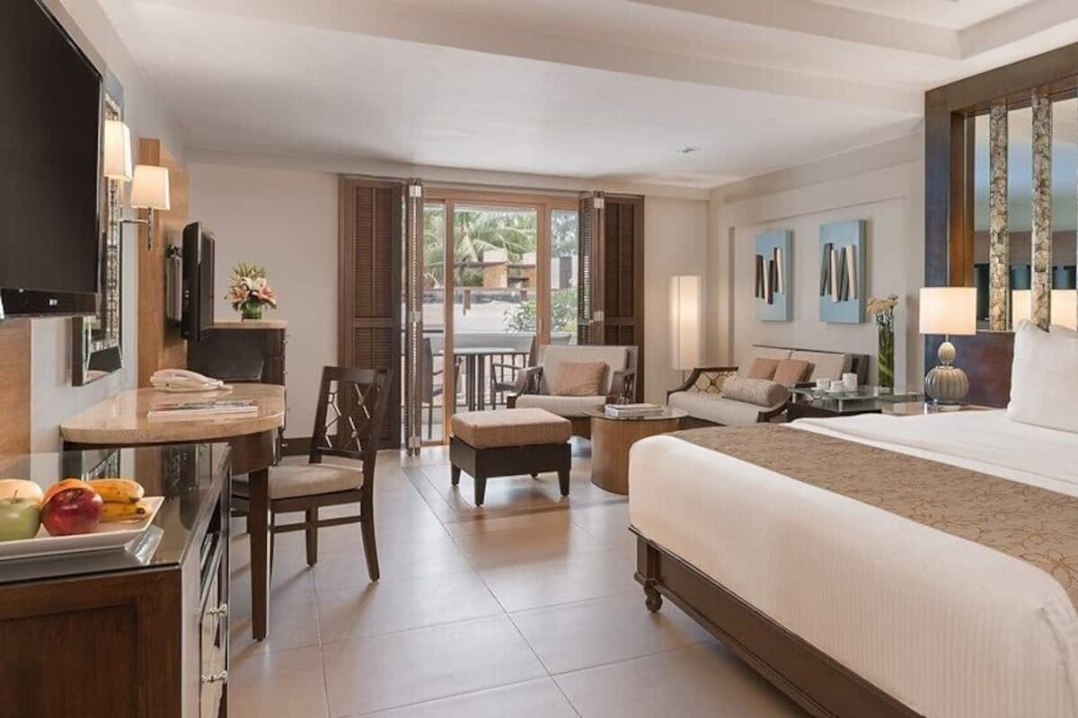 Quarto de hotel com uma cama grande, uma escrivaninha com computador, uma cadeira, um sofá e uma mesa de jantar.