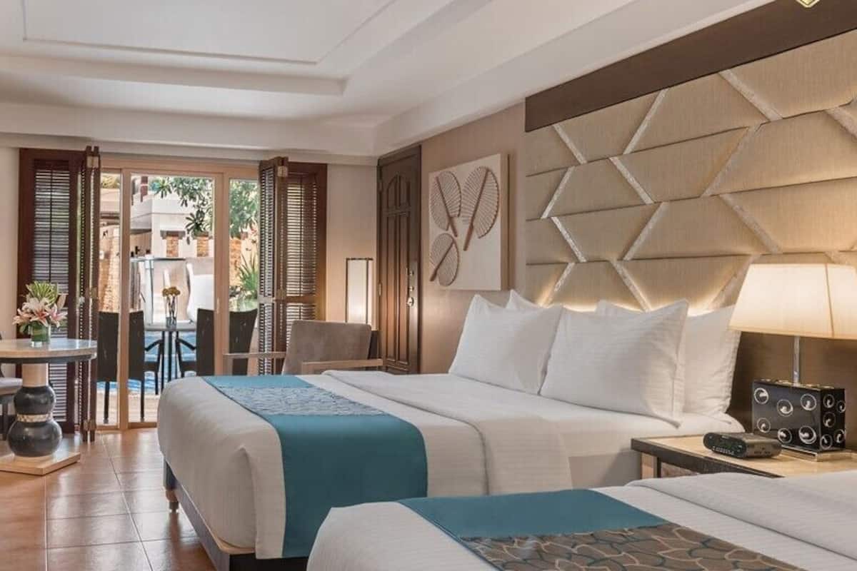 Quarto de hotel com cama, mesa de cabeceira, abajur e escrivaninha com cadeira.