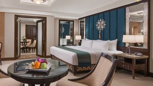 Quarto de hotel com cama, escrivaninha, cadeira, mesa redonda com frutas e televisão.