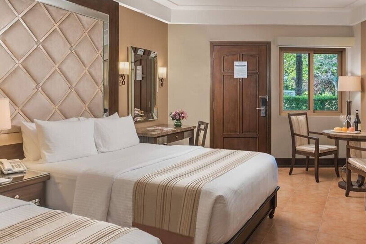 Quarto de hotel com duas camas, uma escrivaninha, televisão e porta para uma varanda.