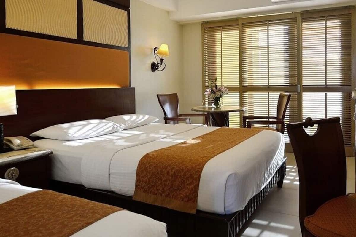 Quarto de hotel com duas camas, uma escrivaninha com cadeira, uma mesa de jantar com frutas e uma televisão.