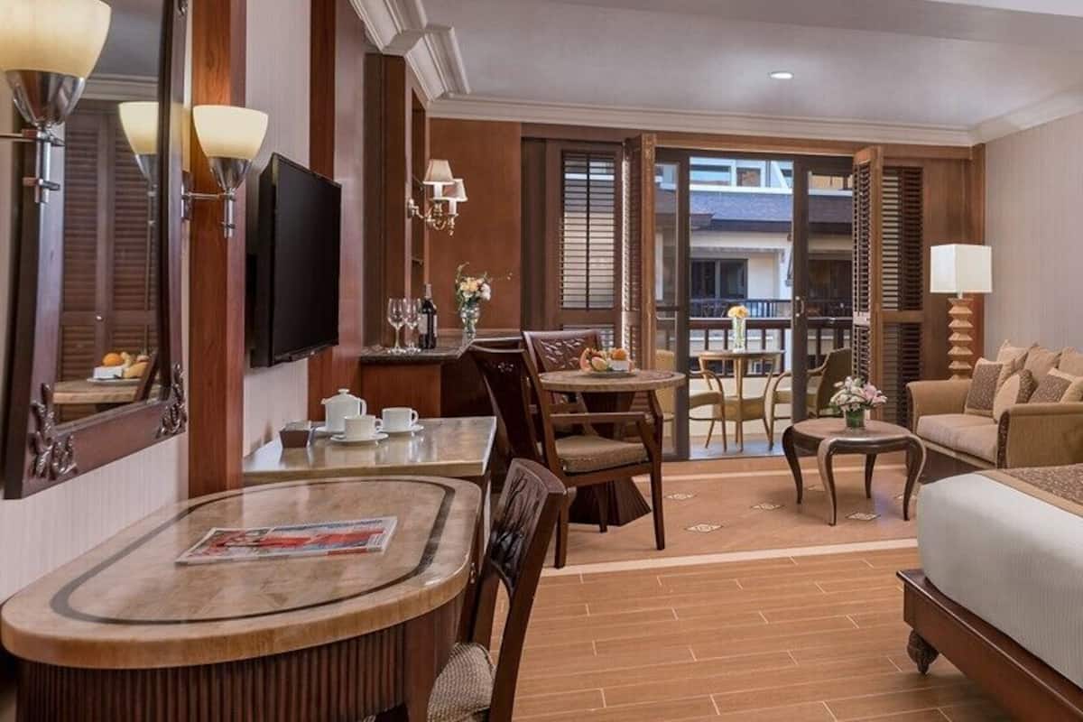Quarto de hotel com uma cama grande, uma escrivaninha com cadeira, uma mesinha e uma televisão.
