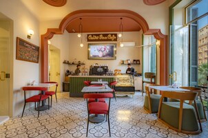 Interior acolhedor de café com decoração vintage, apresentando um balcão com máquina de café, assentos com cadeiras vermelhas e verdes, e um chão estampado.