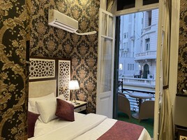 Quarto de hotel com uma cama, mesa de cabeceira, luminária e vista para a varanda externa.