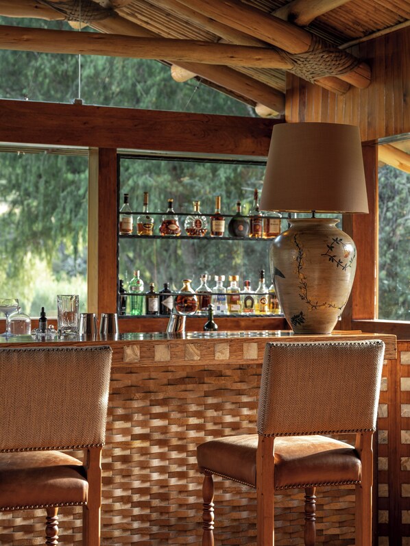 Uma área de bar com móveis de madeira, um vaso grande e prateleiras com garrafas de bebidas.