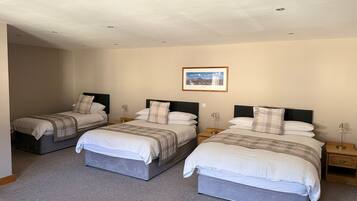 Quarto de hotel com três camas de solteiro, cada uma com cabeceira, mesas de cabeceira e um quadro na parede.