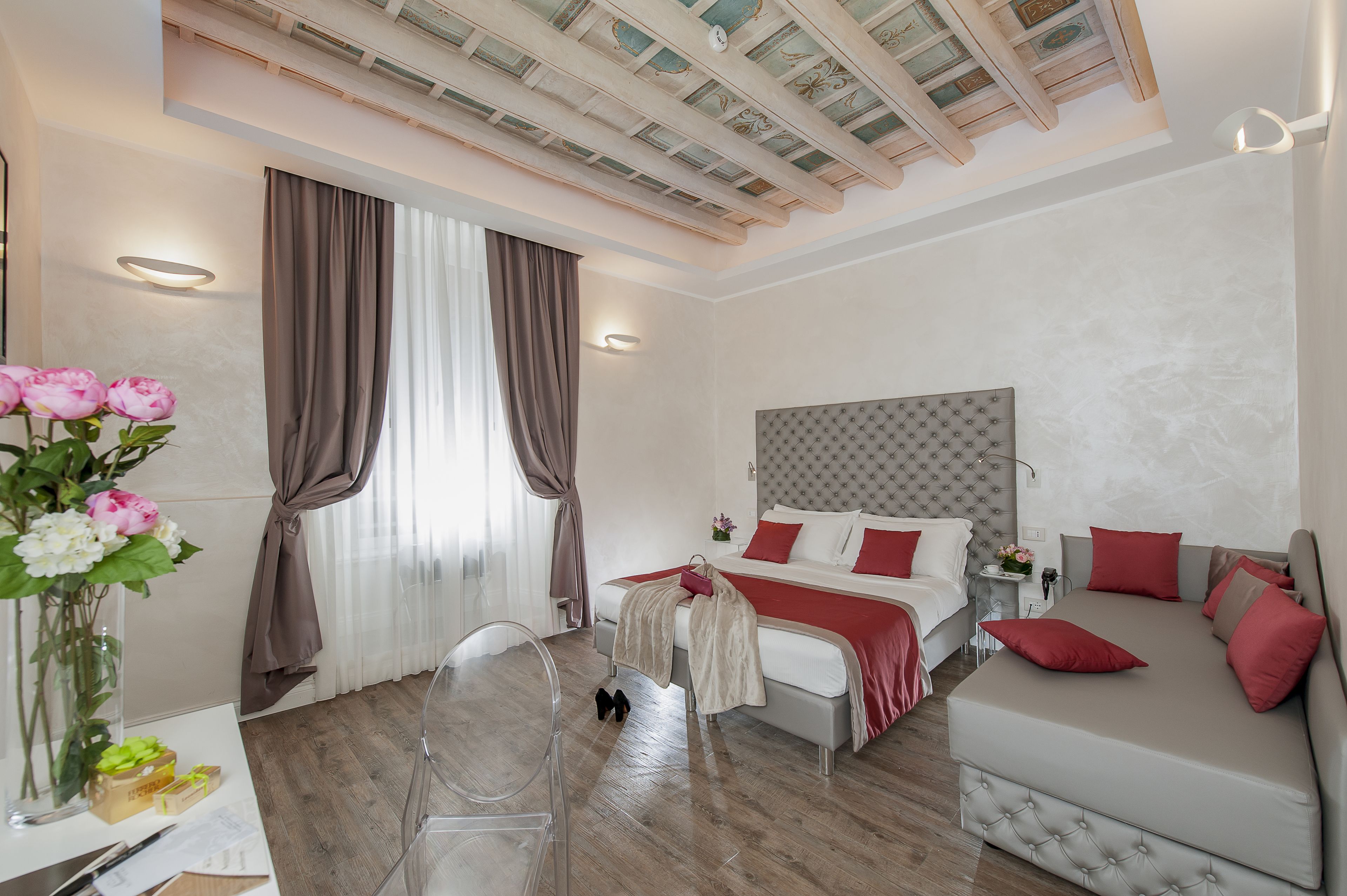 Quarto de hotel moderno com uma cama grande, um sofá, uma mesa com cadeira e um vaso de flores.