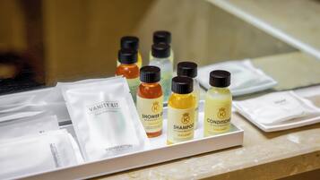Uma bancada de banheiro de hotel com diversos artigos de higiene, incluindo kit de higiene pessoal, gel de banho, shampoo e condicionador.