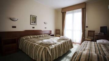 Quarto de hotel com duas camas, cabeceira de madeira, escrivaninha com cadeira e televisão.